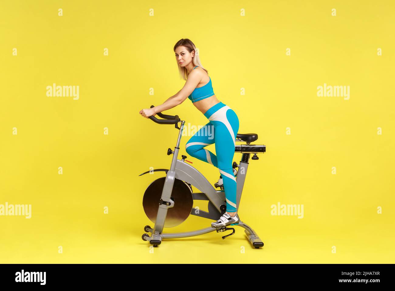 Side view full length of blonde beautiful woman riding exercise bike ...