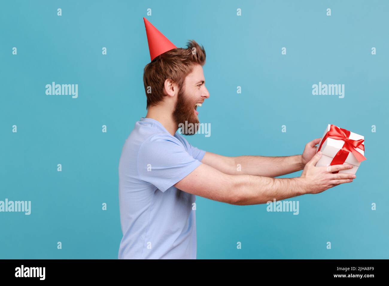 Side view of man in party cone giving birthday gift and smiling ...
