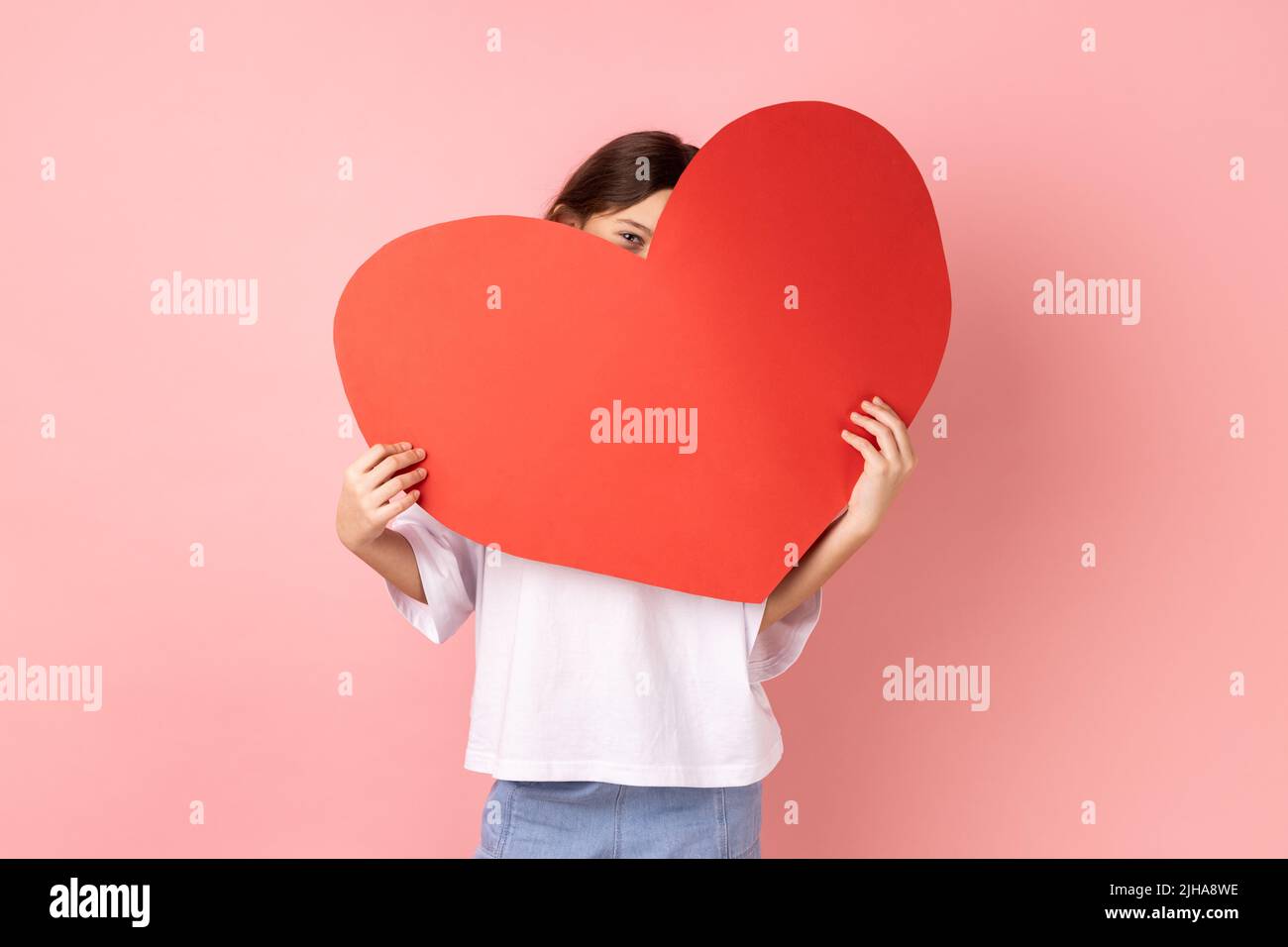 Portrait of little girl in white T-shirt hiding face behind big red ...