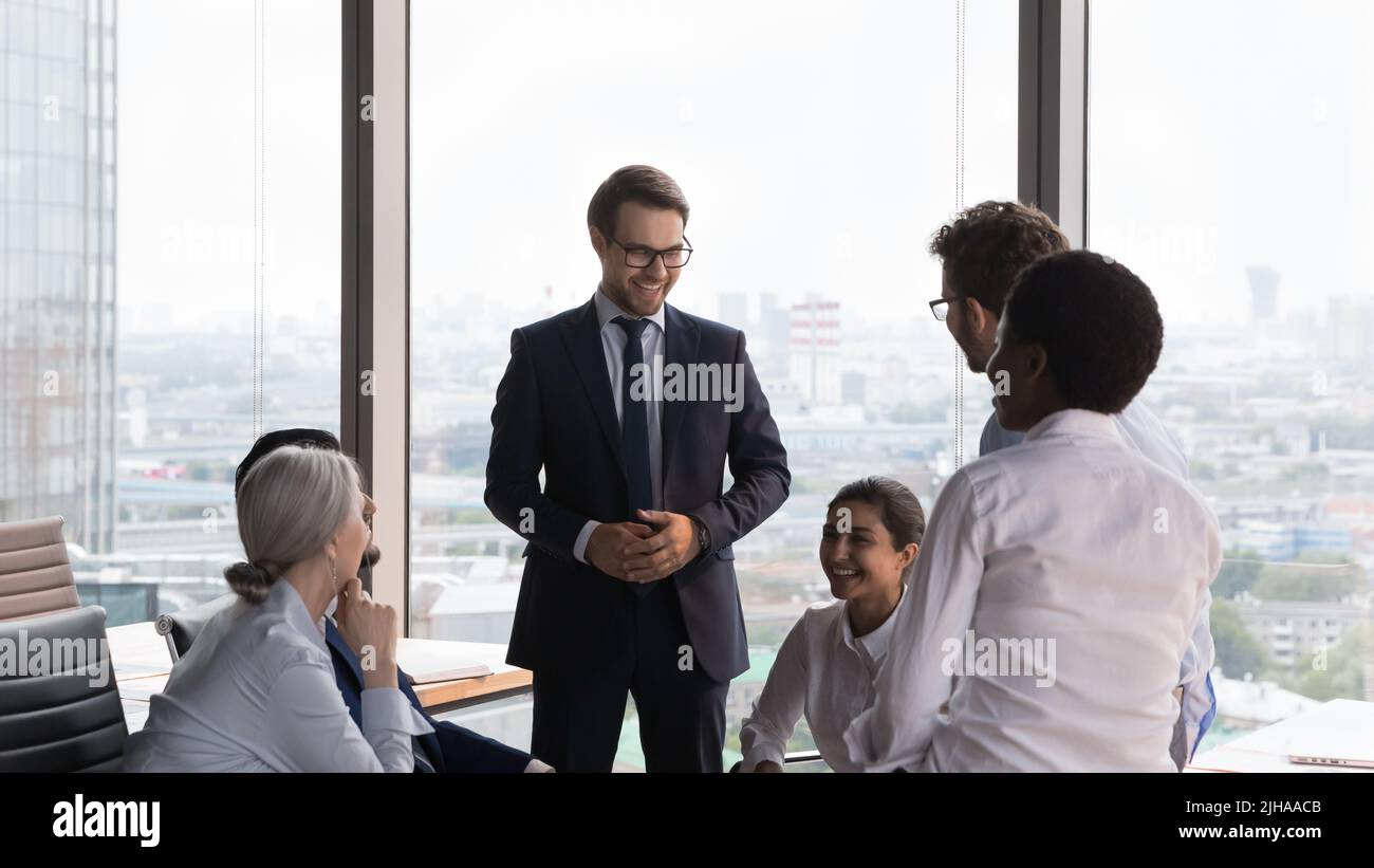 Happy boss holding meeting with multiethnic team, talking to employees ...