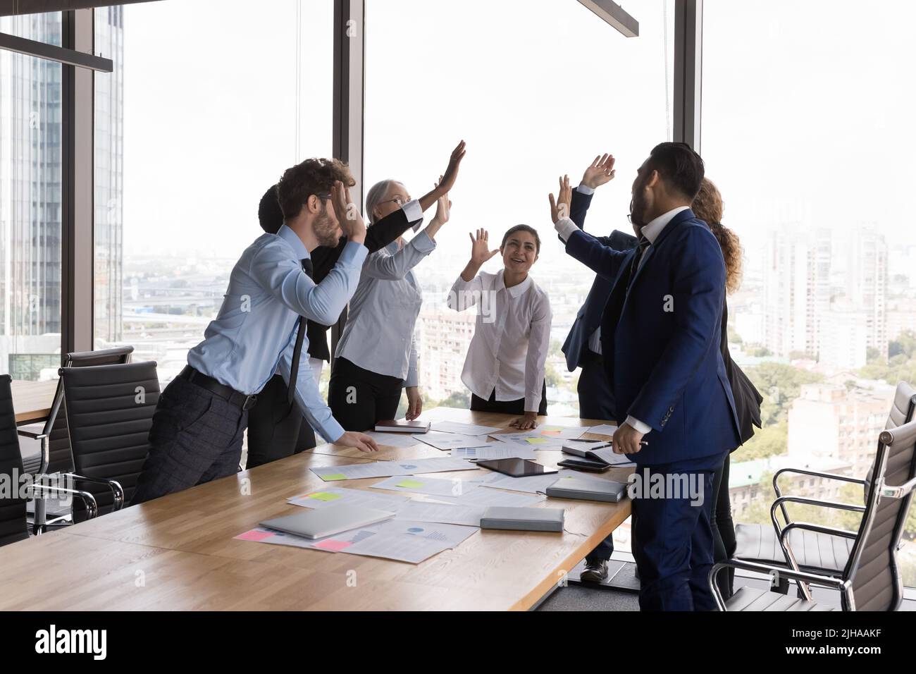 Excited business colleagues giving group high five over meeting table ...