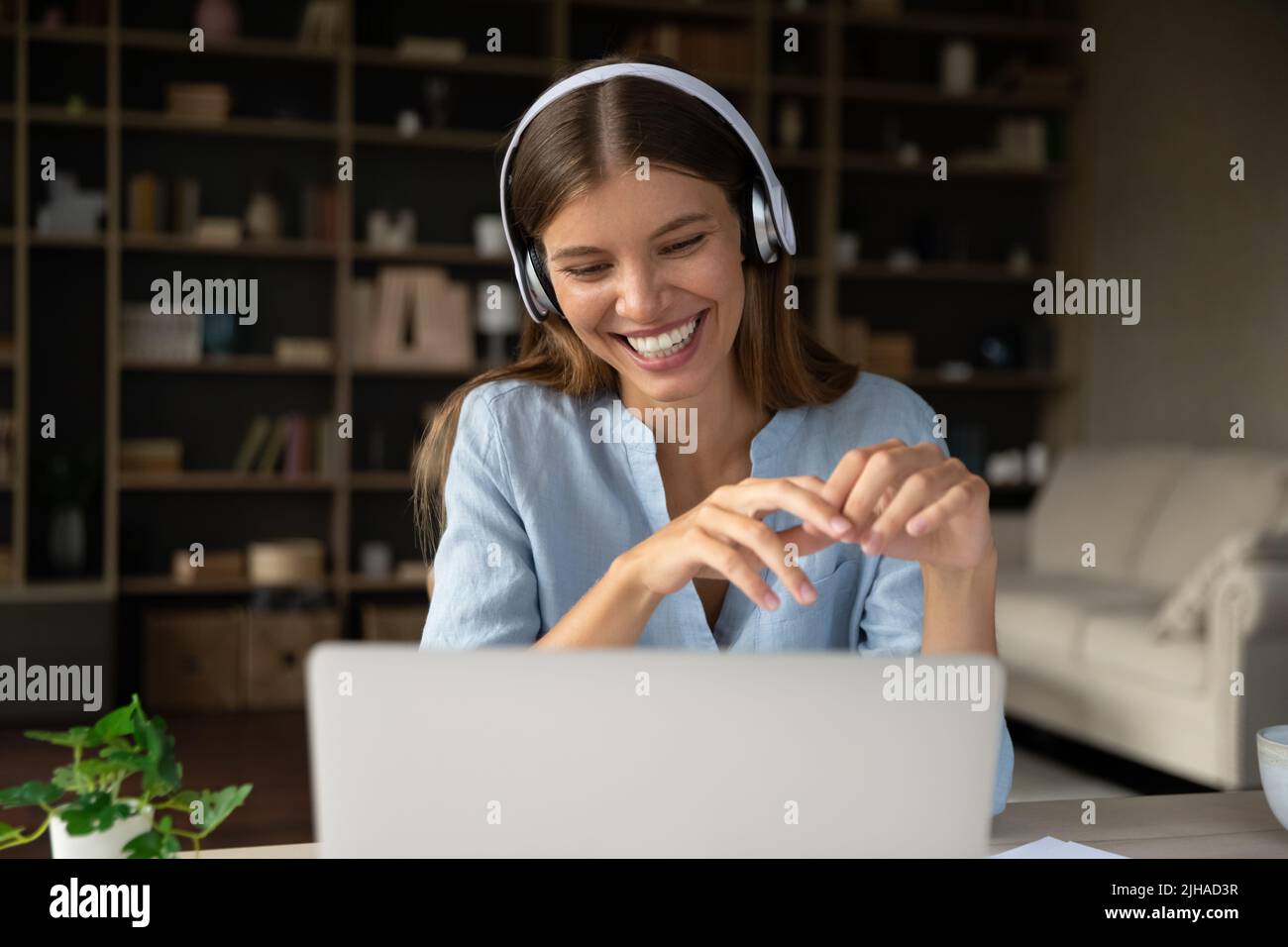 Woman in headphones looks at laptop screen seated at desk Stock Photo ...