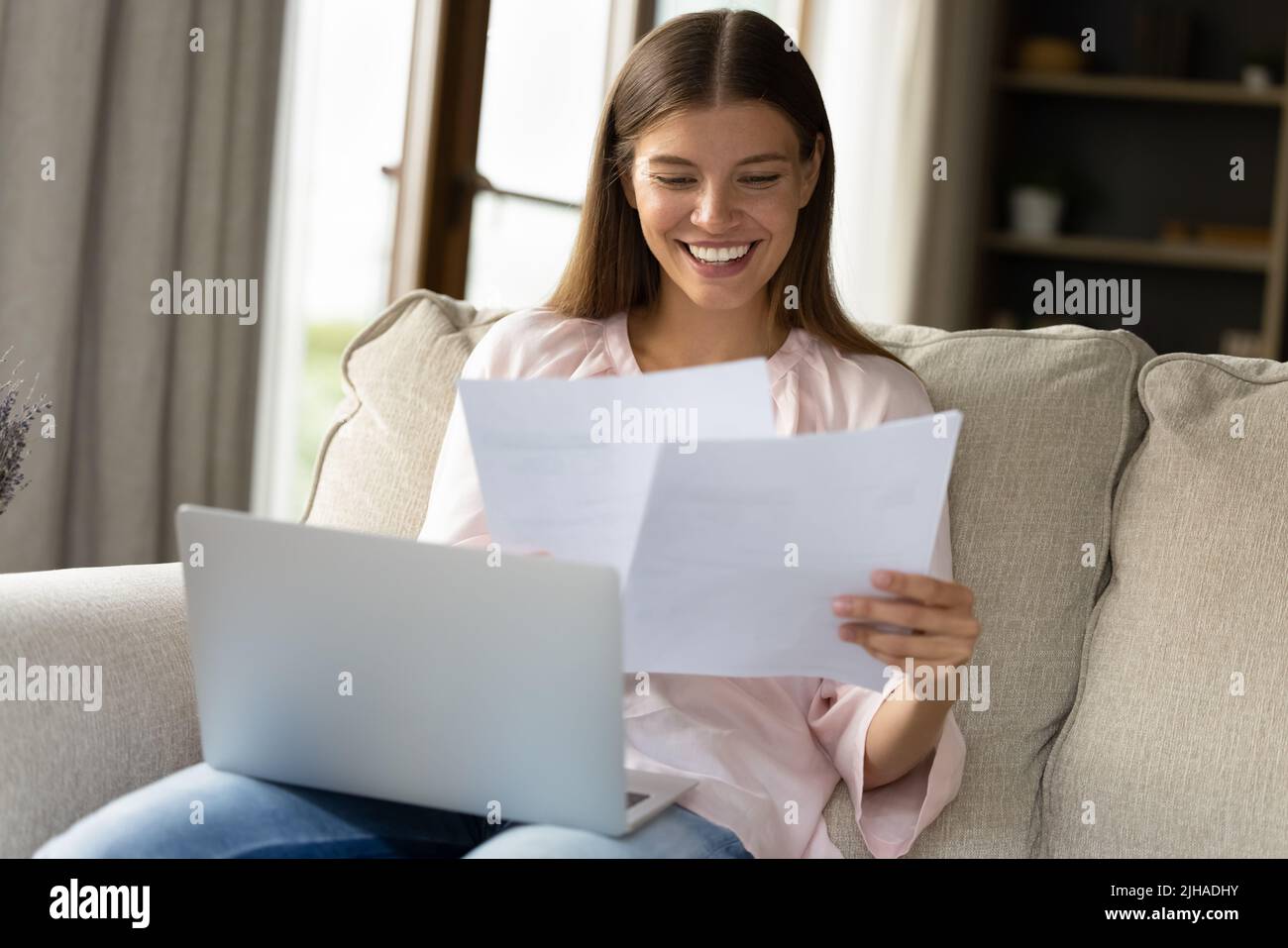 Woman sit on sofa with laptop, smile read paper notification Stock Photo - Alamy