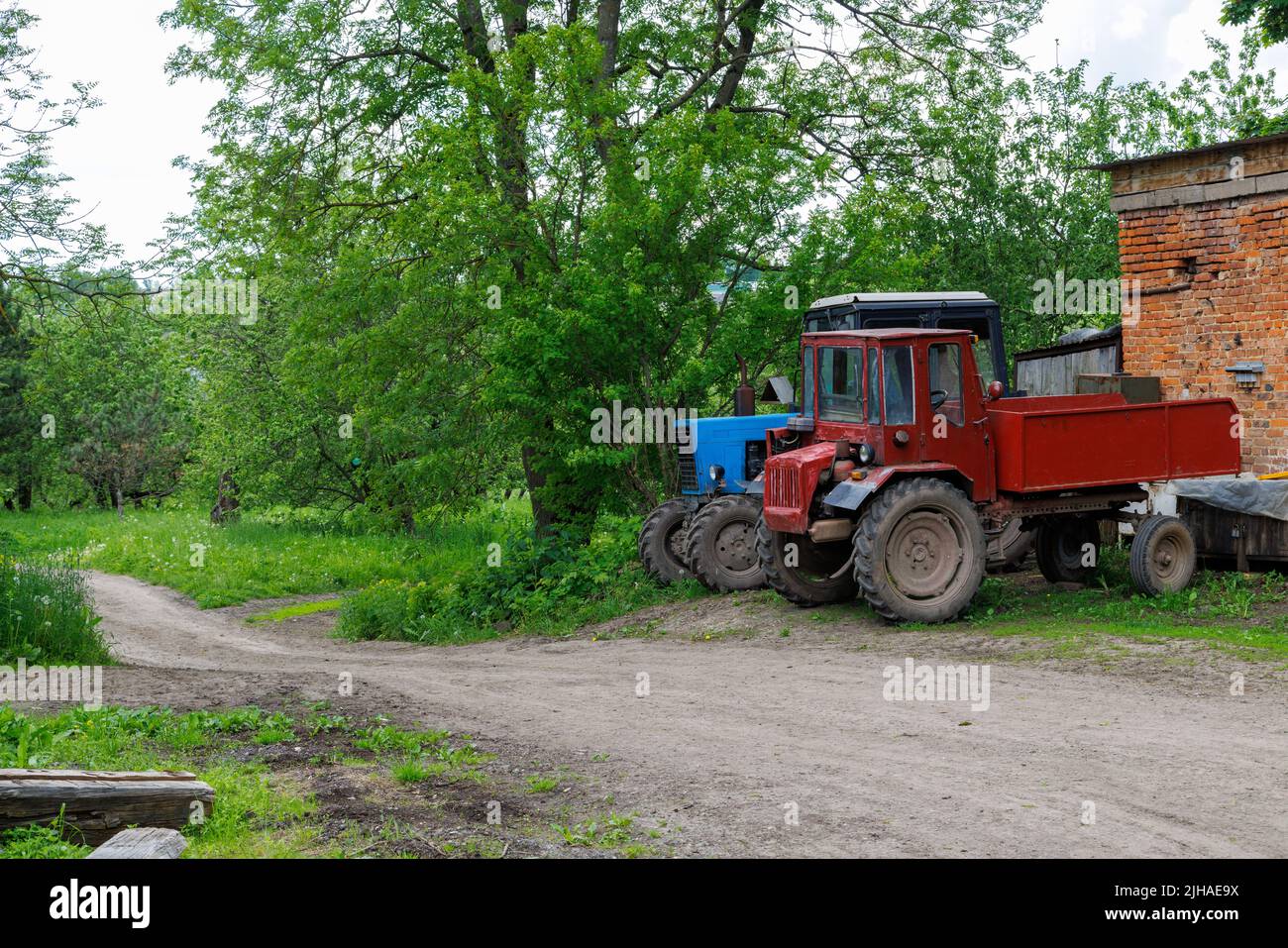 two old soviet tractors near brick building in summer day apple garden ...