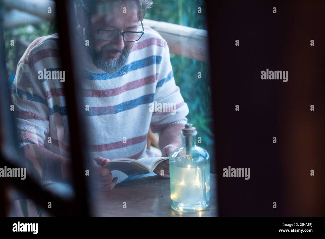 View of a man reading a book through the glass window from inside home ...