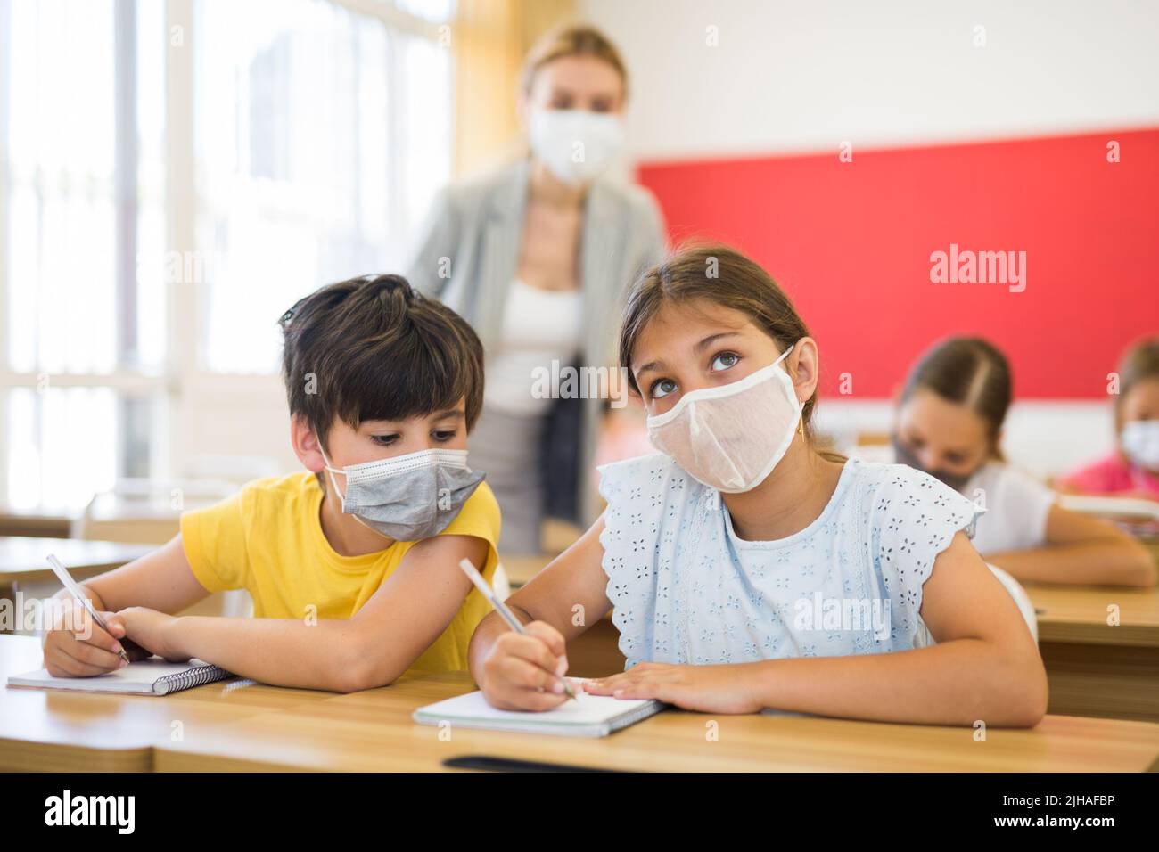 School boy and girl in face masks listening to teacher at lesson in ...
