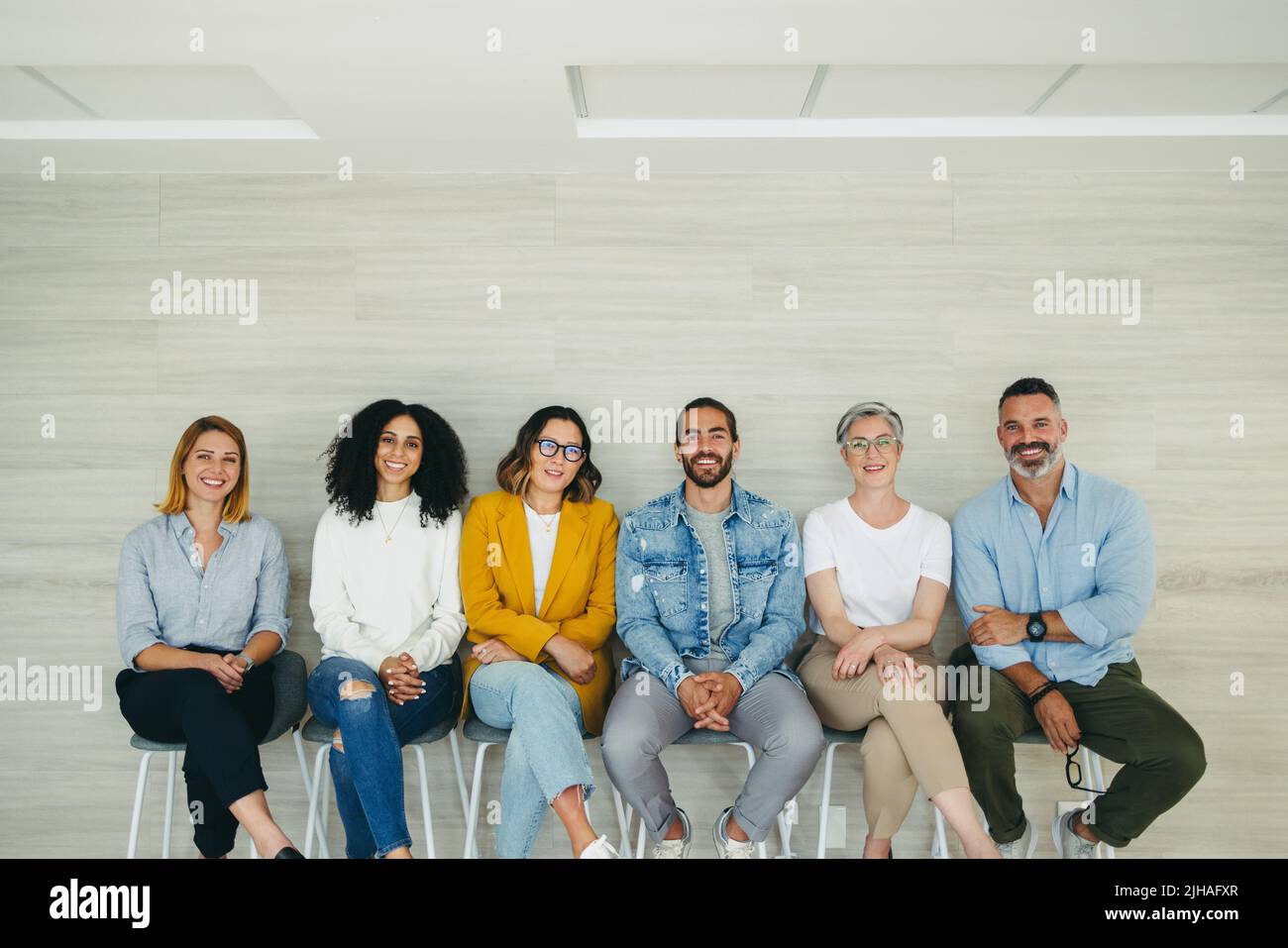Happy job applicants smiling at the camera while sitting in line for an ...
