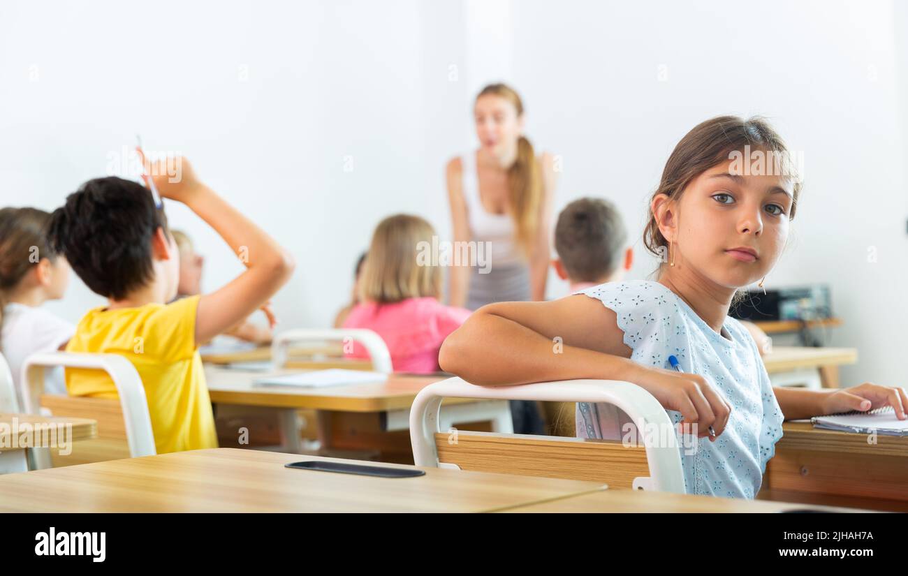 Positive tween schoolgirl sitting at school desk at lesson in class ...