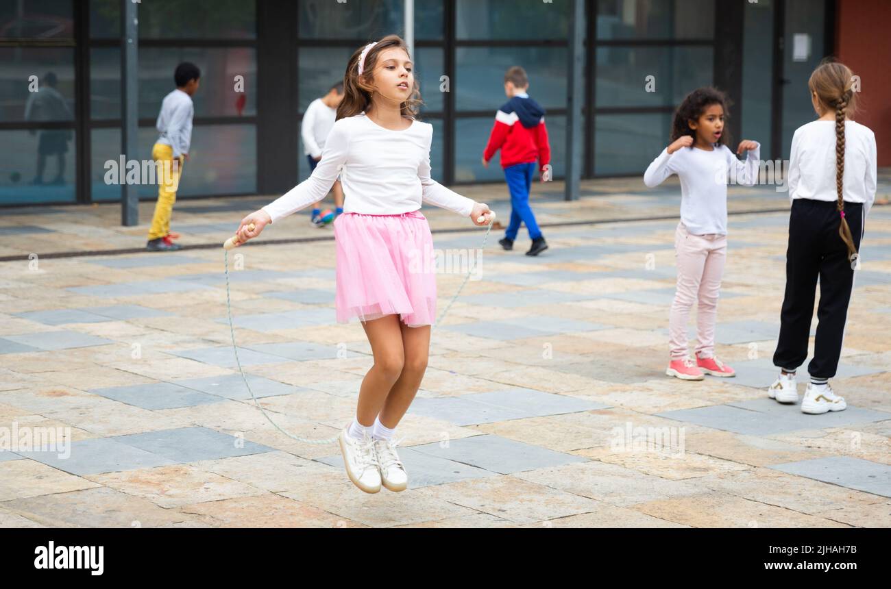 Schoolgirl jumping game by rubber band, kids friends on background ...