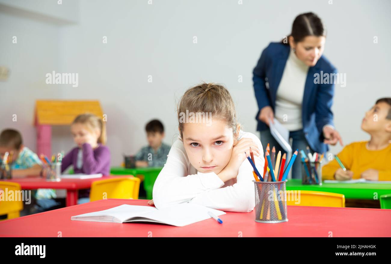 Upset schoolgirl sitting at a desk in classroom elementary school Stock ...