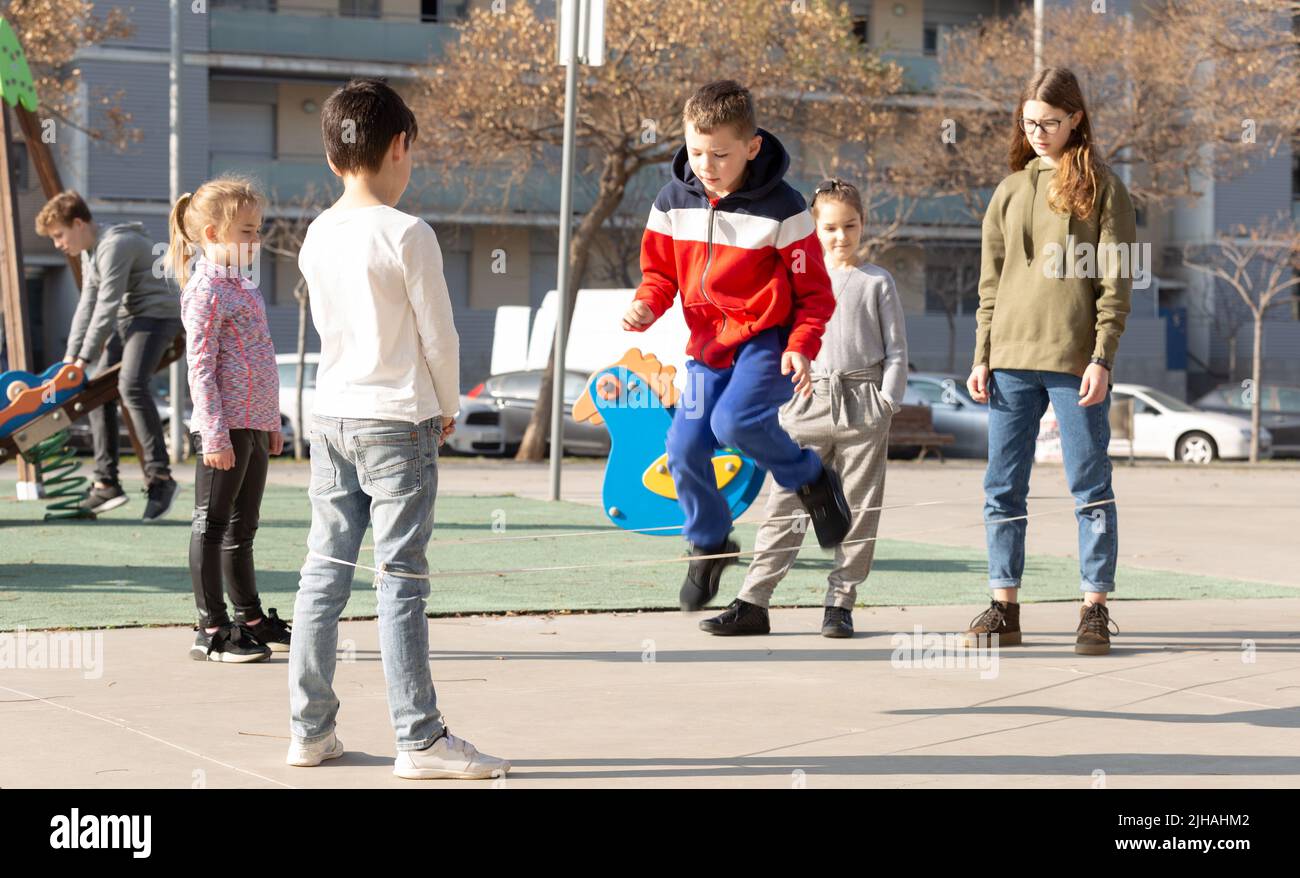 Energetic kids playing and skipping on elastic jumping rope in european ...