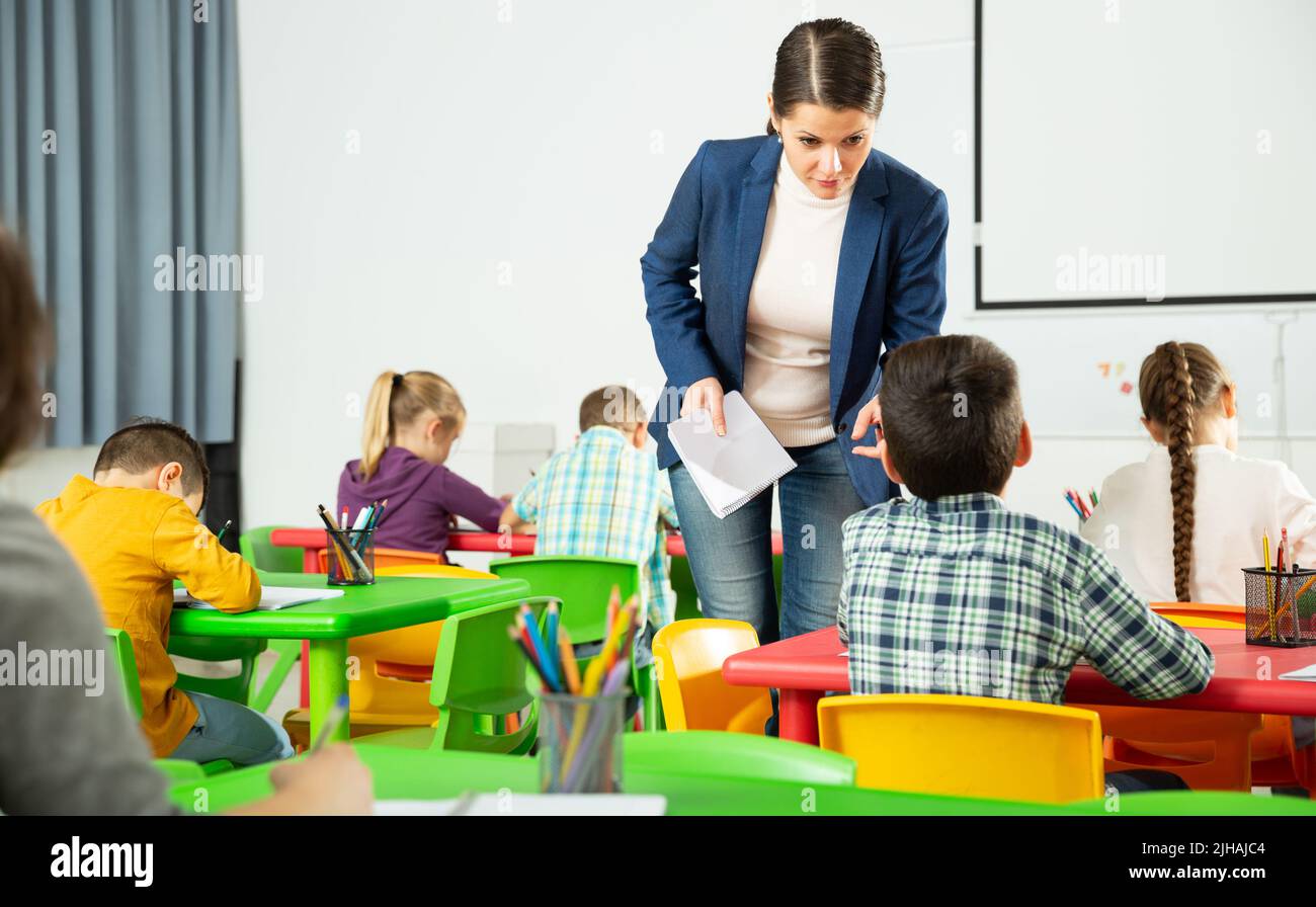 Friendly teacher woman helping boy during lesson in schoolroom Stock ...