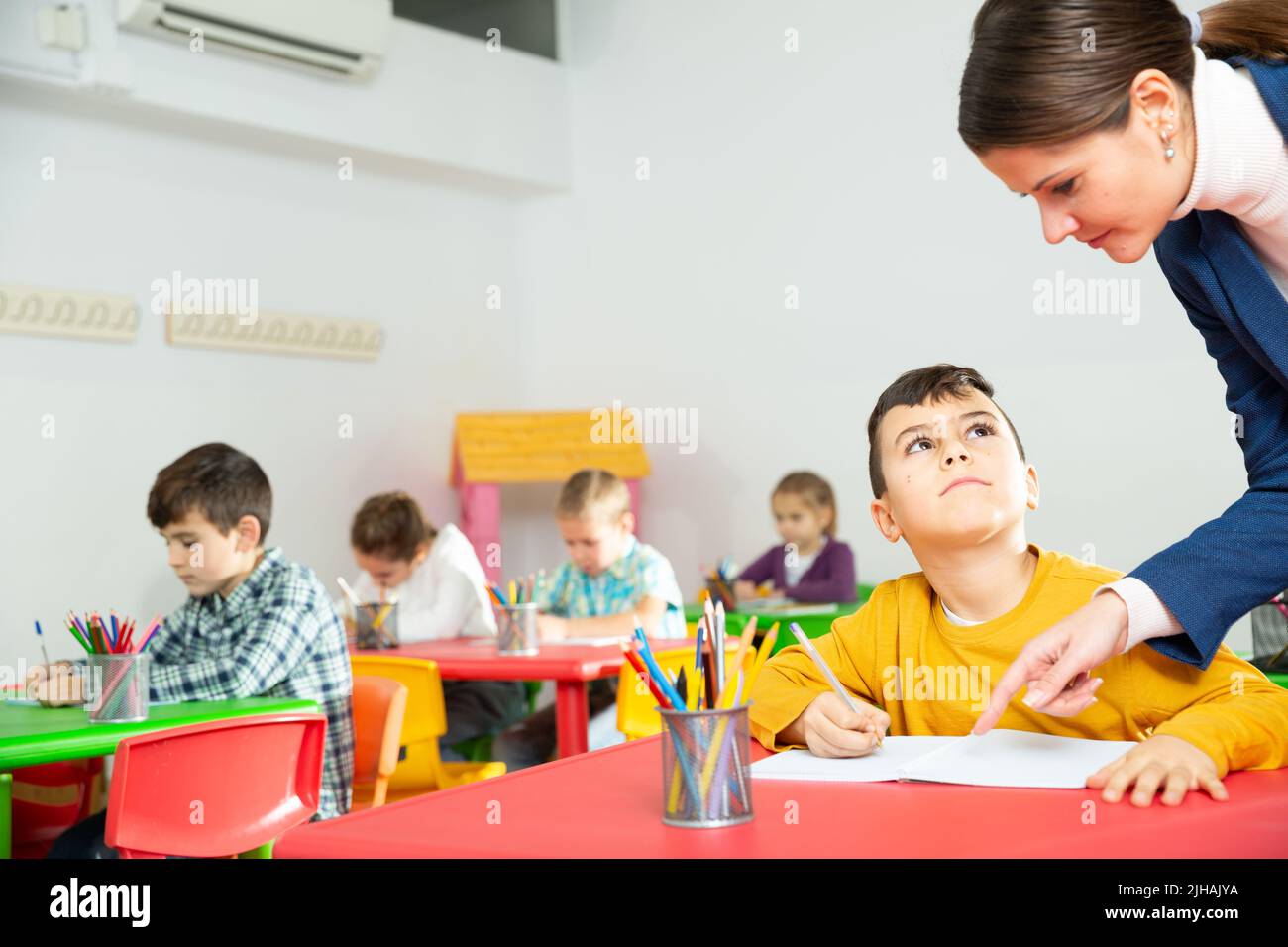 Friendly teacher woman helping boy during lesson in schoolroom Stock ...