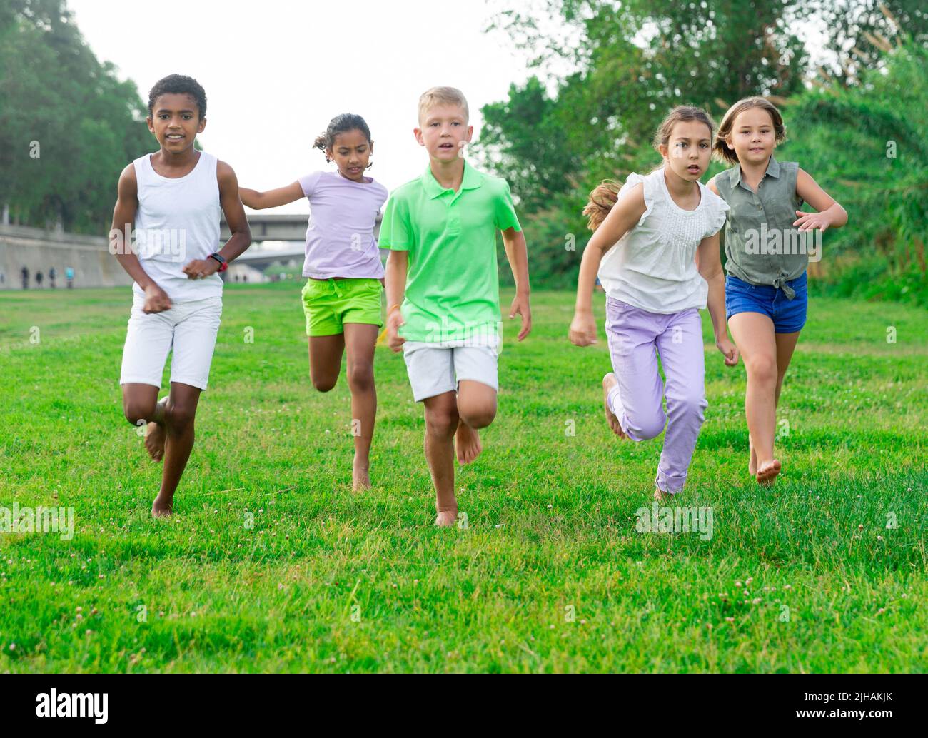 Multiracial group of cheerful tweens running together in city park ...