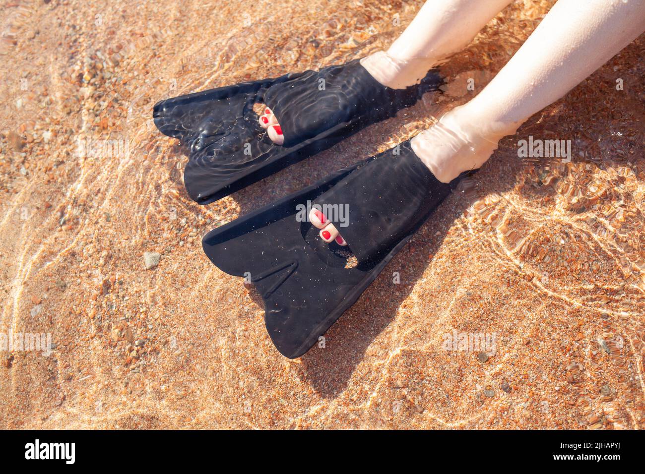 A woman in black flippers splashes near the shore. Fins stick out of ...