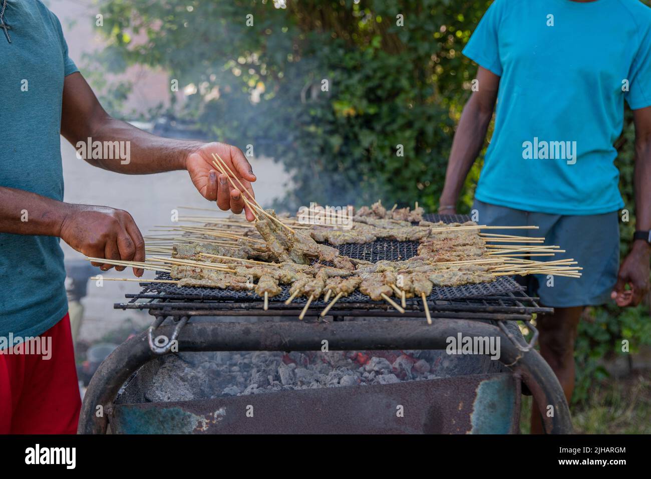 Close-up of a grill with some meat skewers, two african men are cooking ...