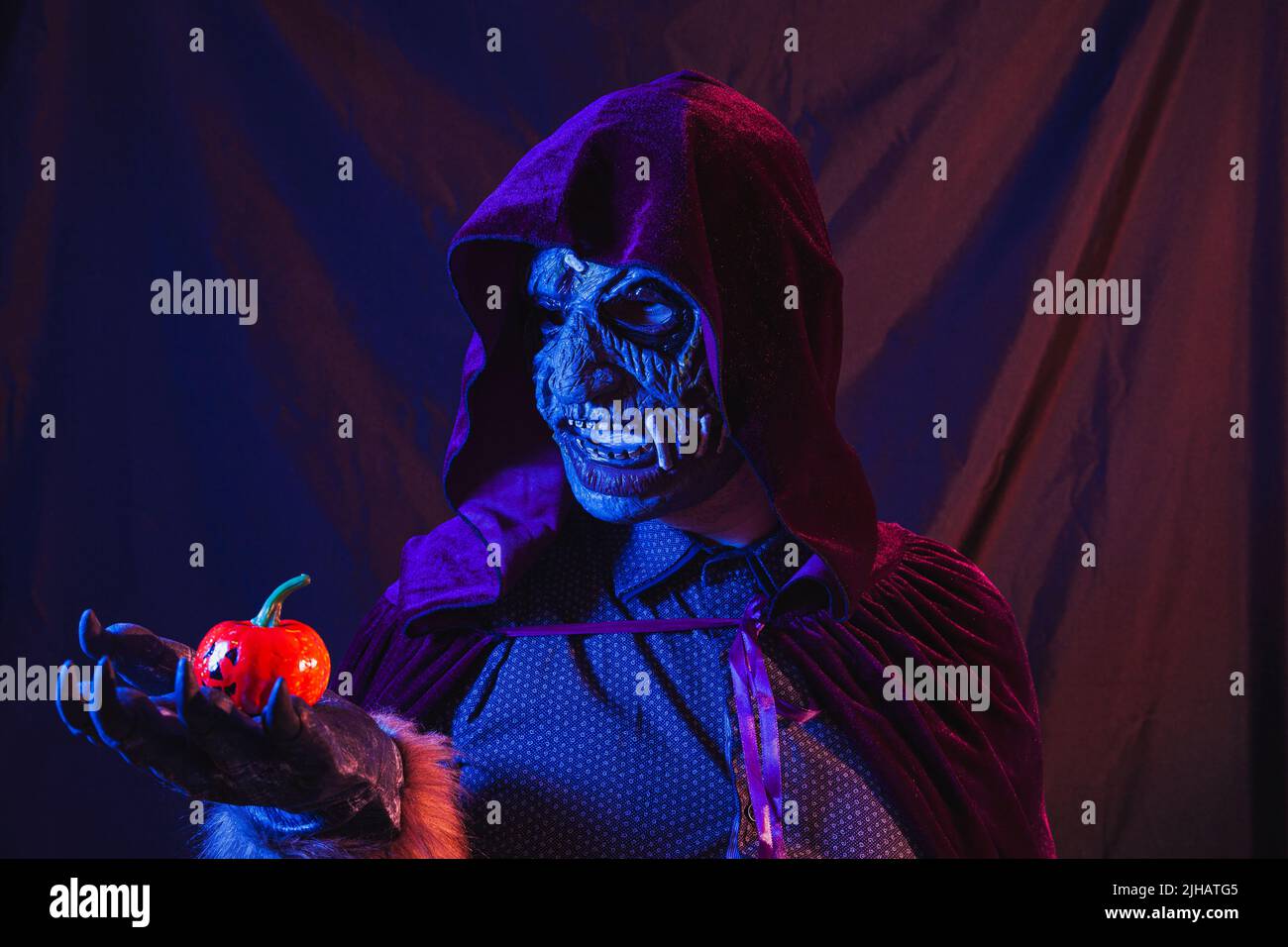 Portrait of a zombie dressed in a shirt and hooded cape holding a small ...