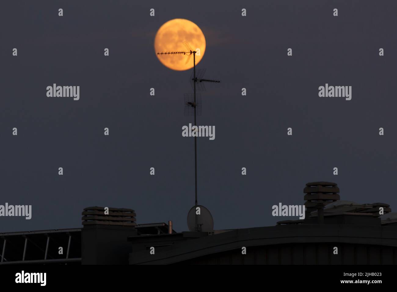 Full blood red moon in a city sky, tv antennas are visible in the ...