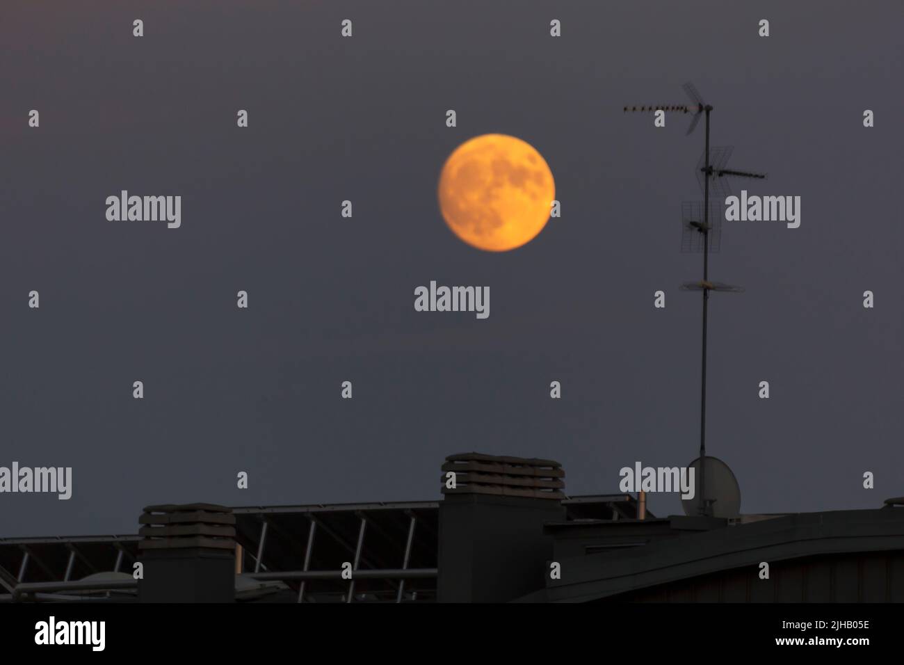 Full blood red moon in a city sky, tv antennas are visible in the ...