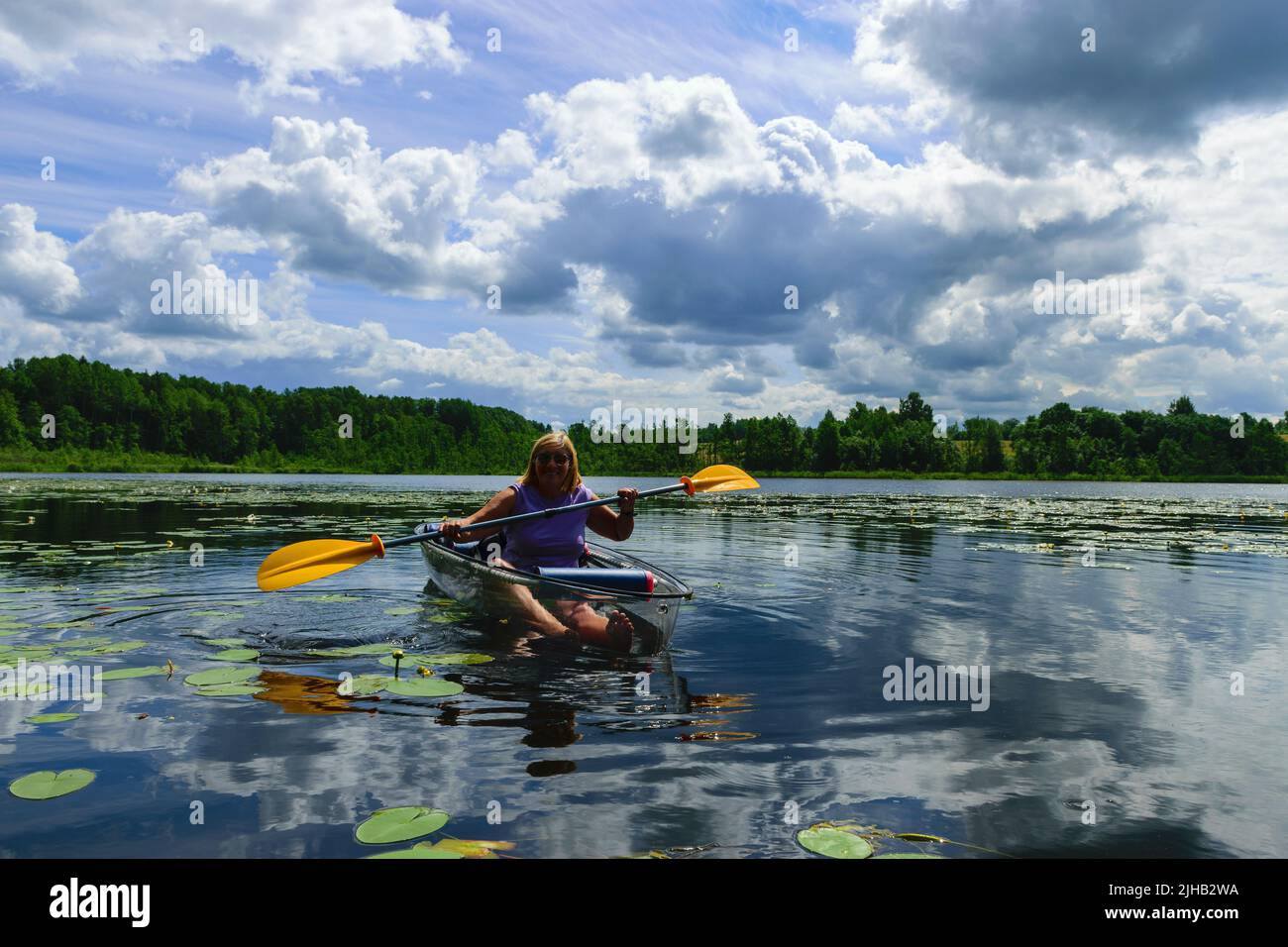 woman enjoying weekend rowing on transparent boat in small lake, bright ...