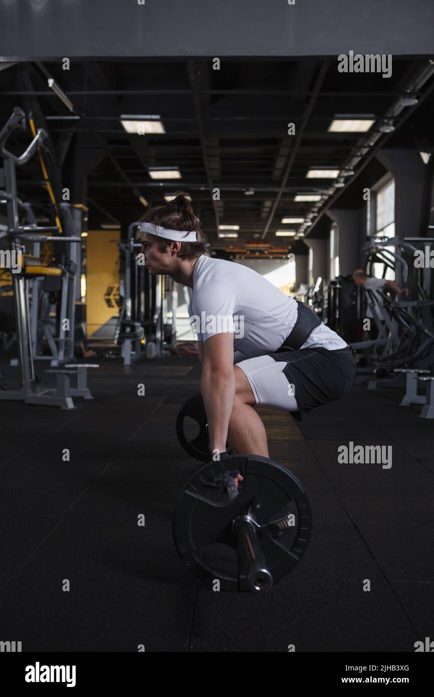 Vertical profile shot of a sportsman doing weightlifting workout with ...