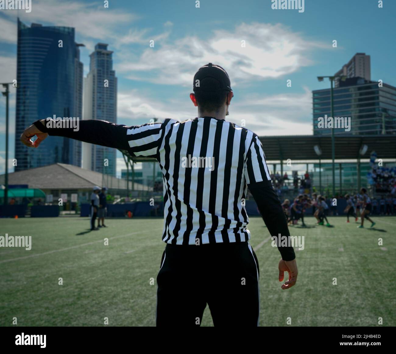 A rear view of a male referee in a field raising his left arm to the ...