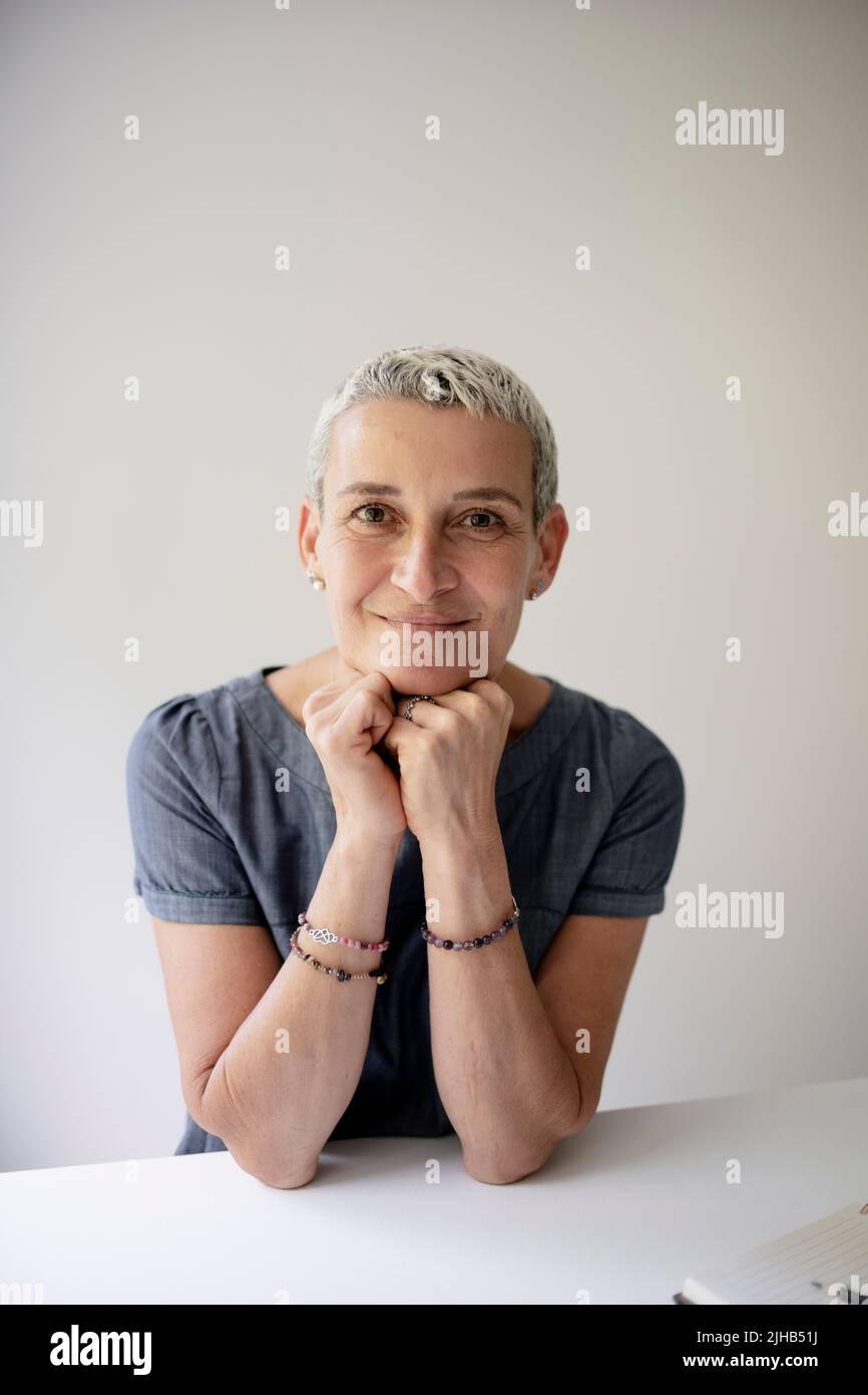 pretty middle aged woman with grey dress sits in white office by desk ...