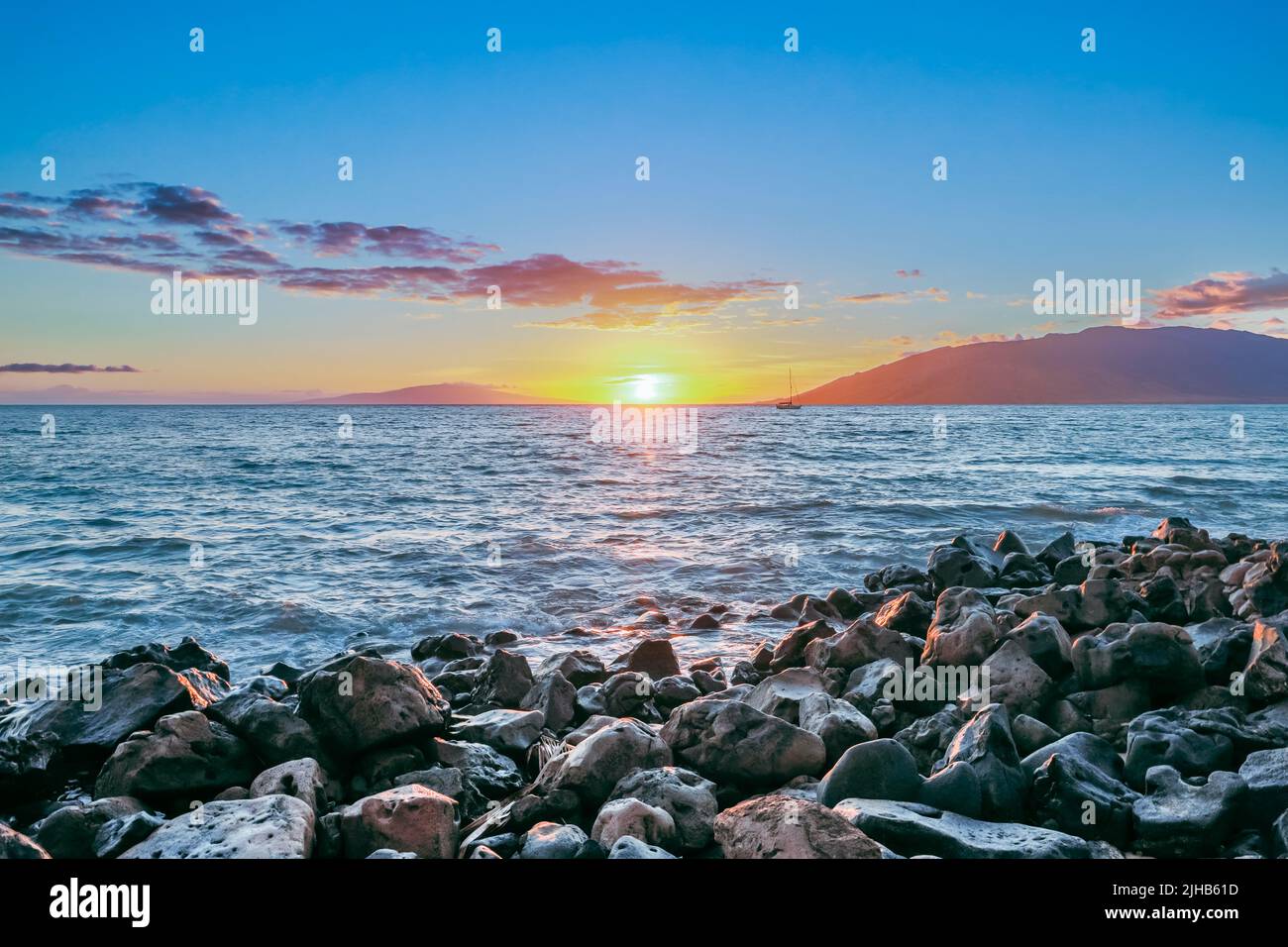 Maui Hawaii at sunset with a low sun and rocks and a mountain Stock ...