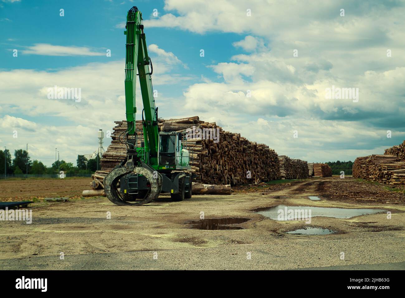 An old green log handling machine and a huge pile of logs in a rural ...