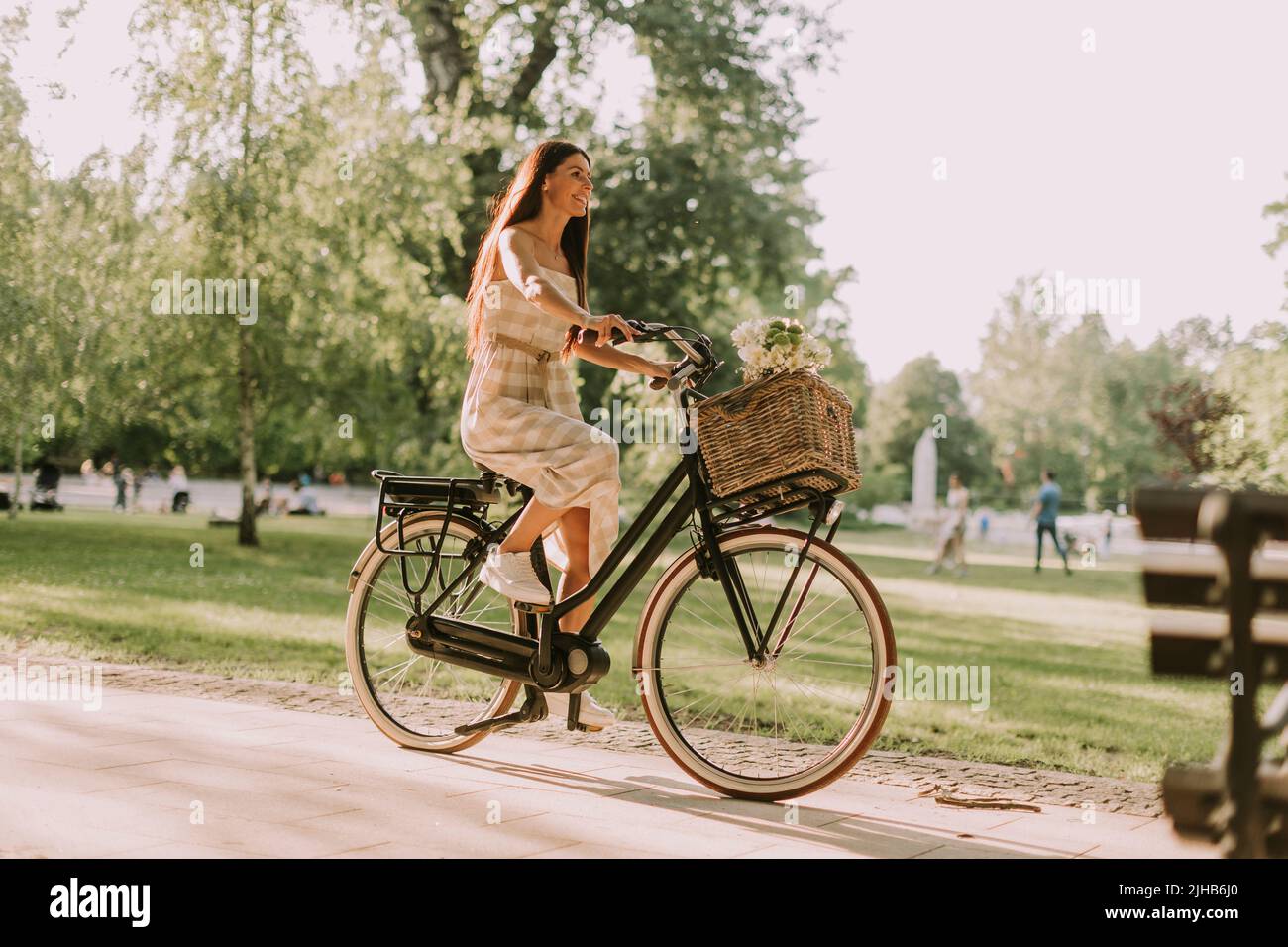 Pretty young woman riding electric bike with flowers in the basket ...