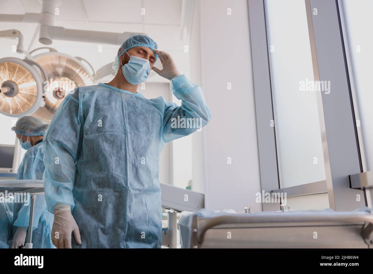 Tired professional surgeon in mask standing in operating room after ...