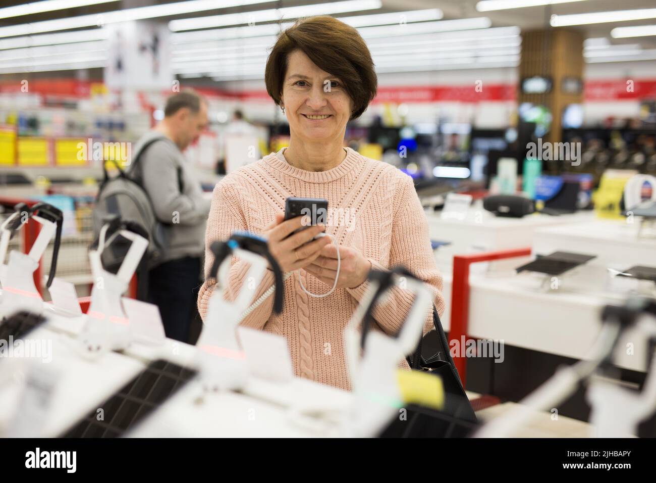 Mature woman choosing smartphone in electronic shop Stock Photo - Alamy