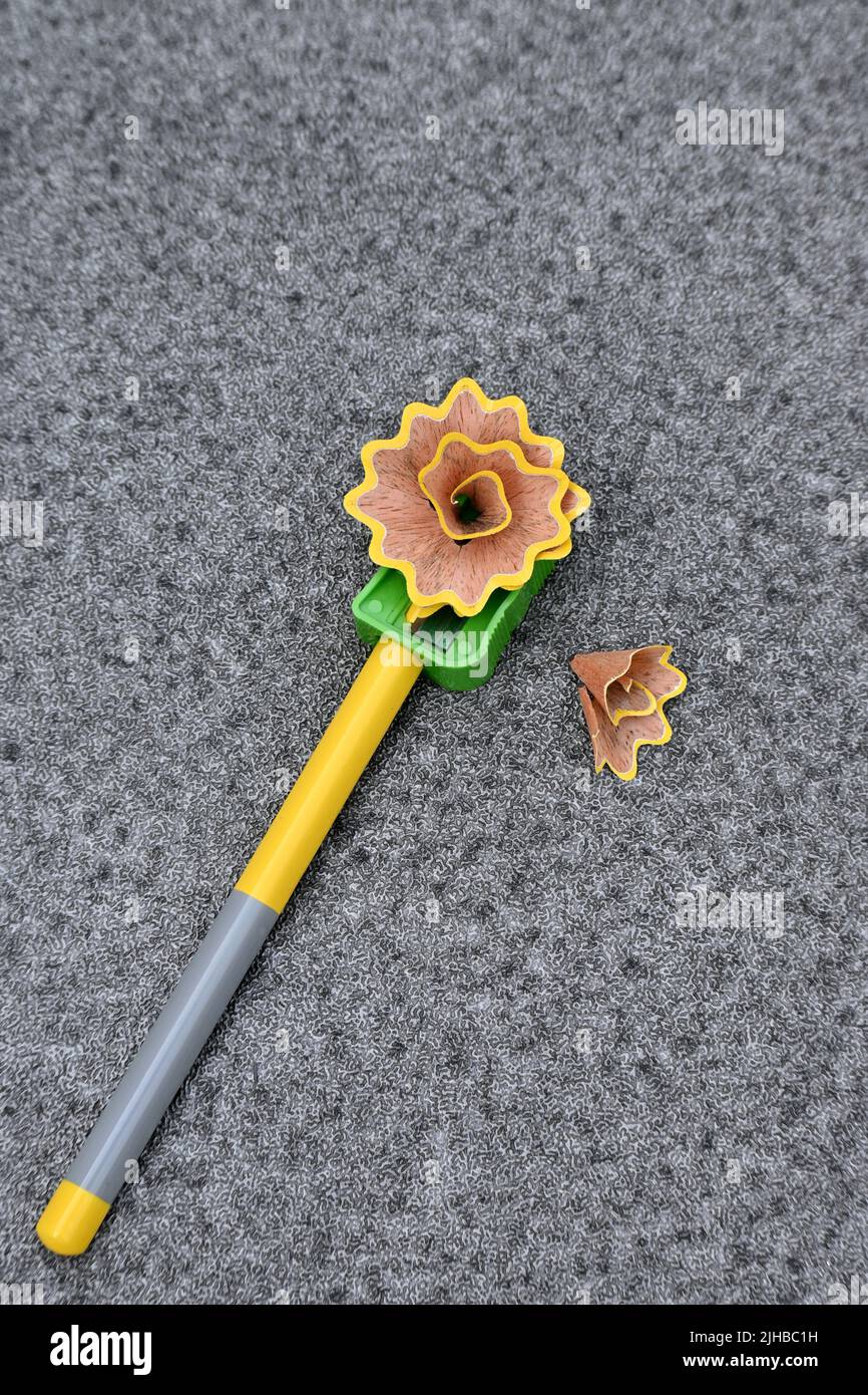 A vertical shot of a yellow wooden pencil with a green sharpener and ...