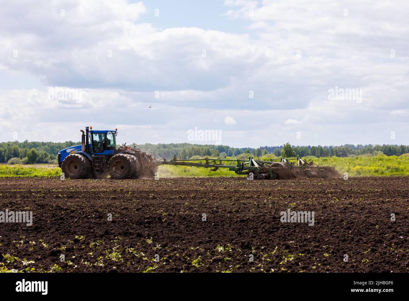 Blue tractor with double wheels pulling disc harrow with roller basket ...