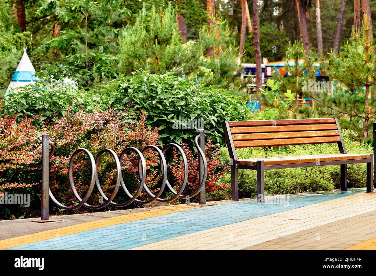 Wooden bench and bike rack in a green city park with rides and trees ...
