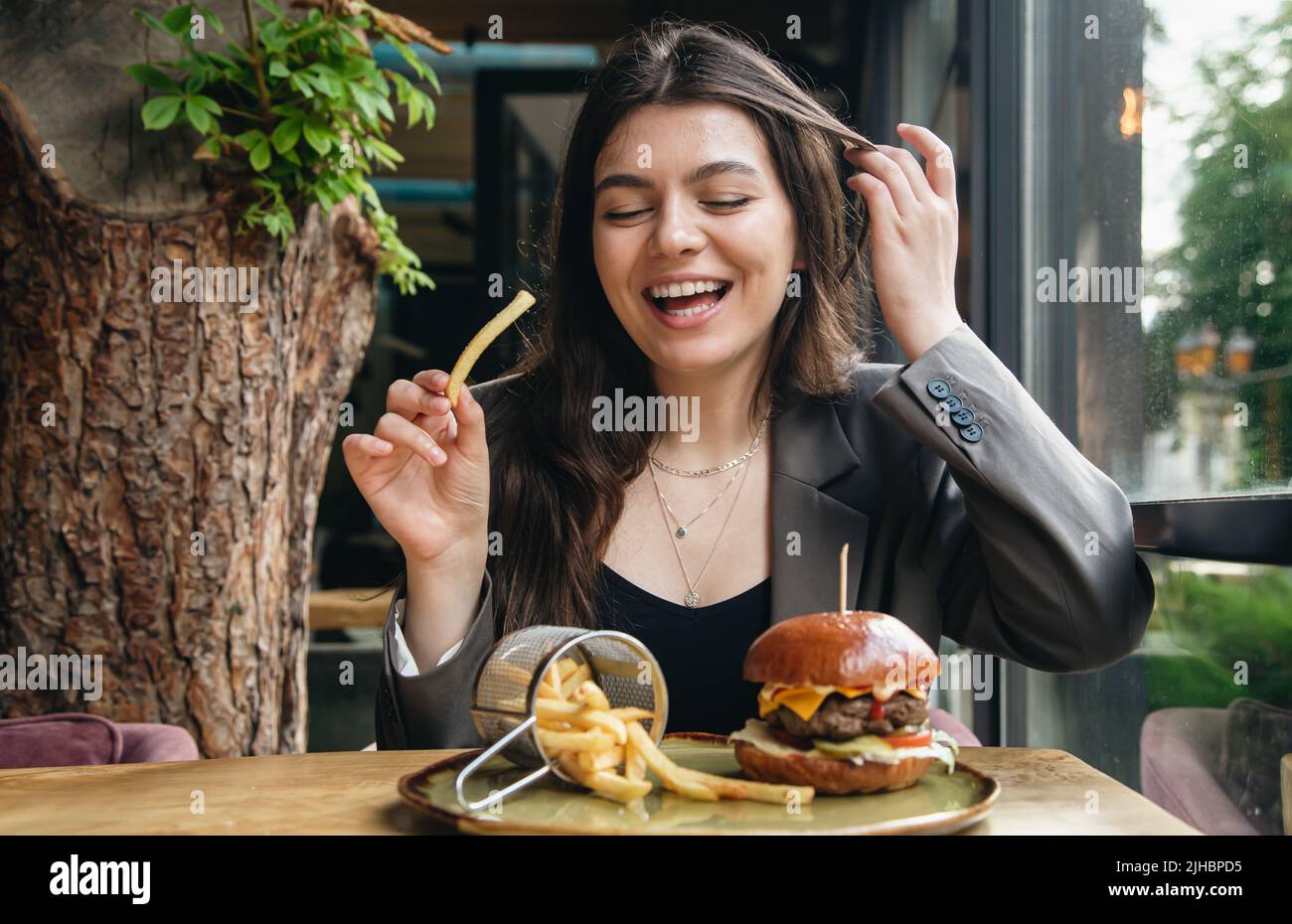 Attractive young woman eating french fries and a burger in a restaurant ...