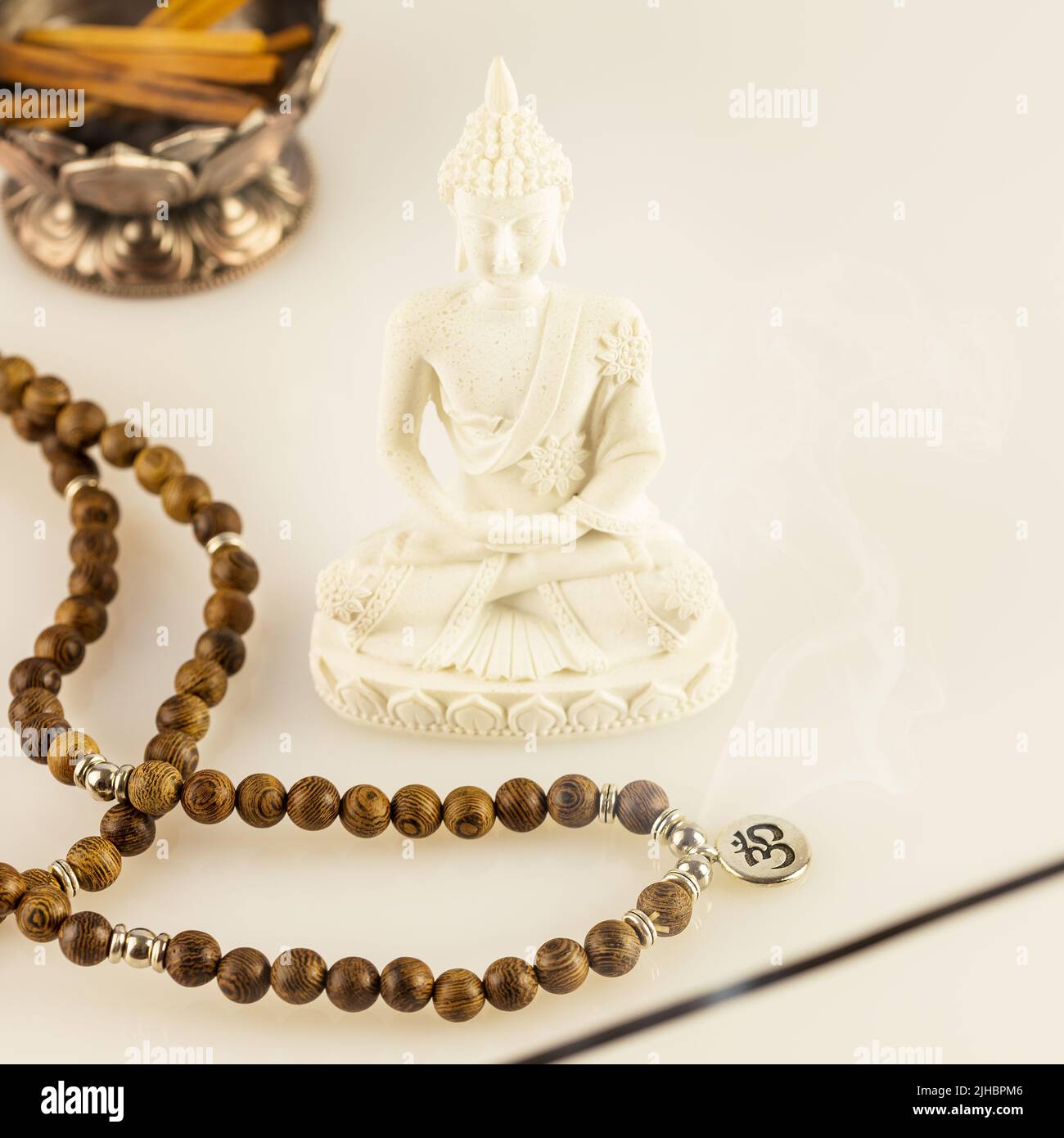 Buddha statue, prayer beads with symbol OM and aroma sticks on a white ...