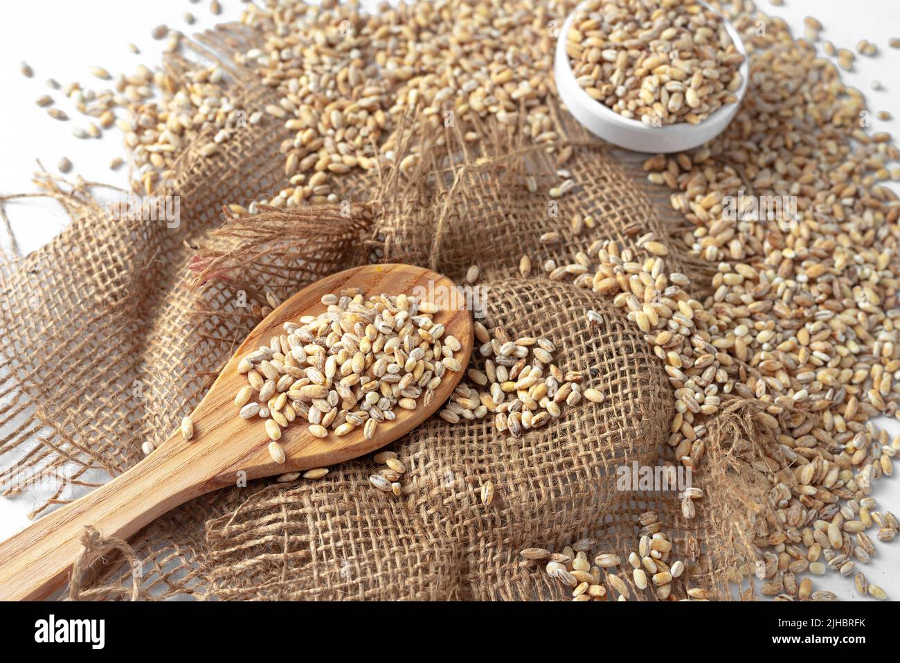Barley on a light background. A pile of dry barley on a wooden spoon ...