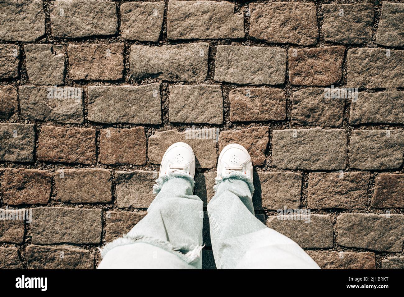 Female legs in jeans and white sneakers on paving stones. Teenage feet ...