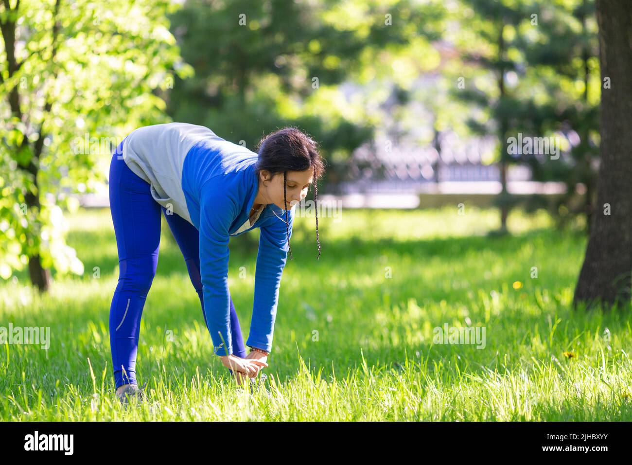 Photo of a 35-year-old woman is warming up in city park. She stretching and warming up the ...