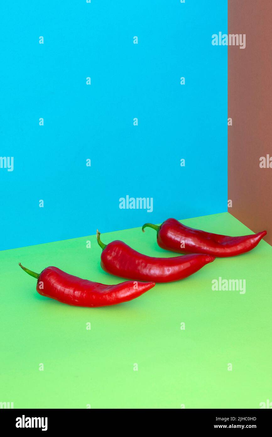 Still life with three red peppers in the corner on a colored background ...