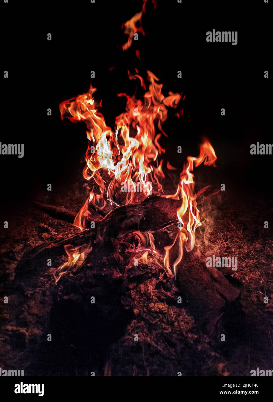 A vertical closeup of campfire with flames and smoke during the night ...