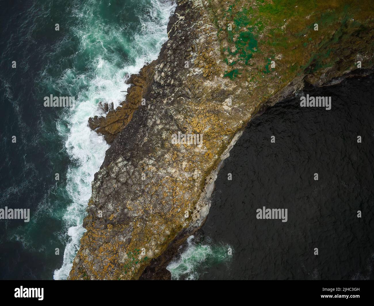 Rocky ocean coast. Dark turquoise water with white foamy waves beats ...