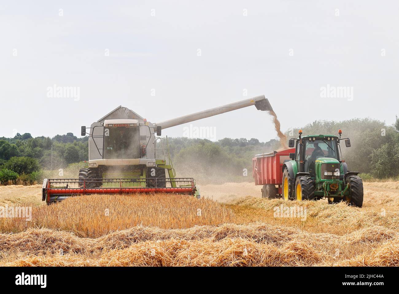 A Claas Lexion 440 combine harvester loading a John Deere 6920s tractor ...