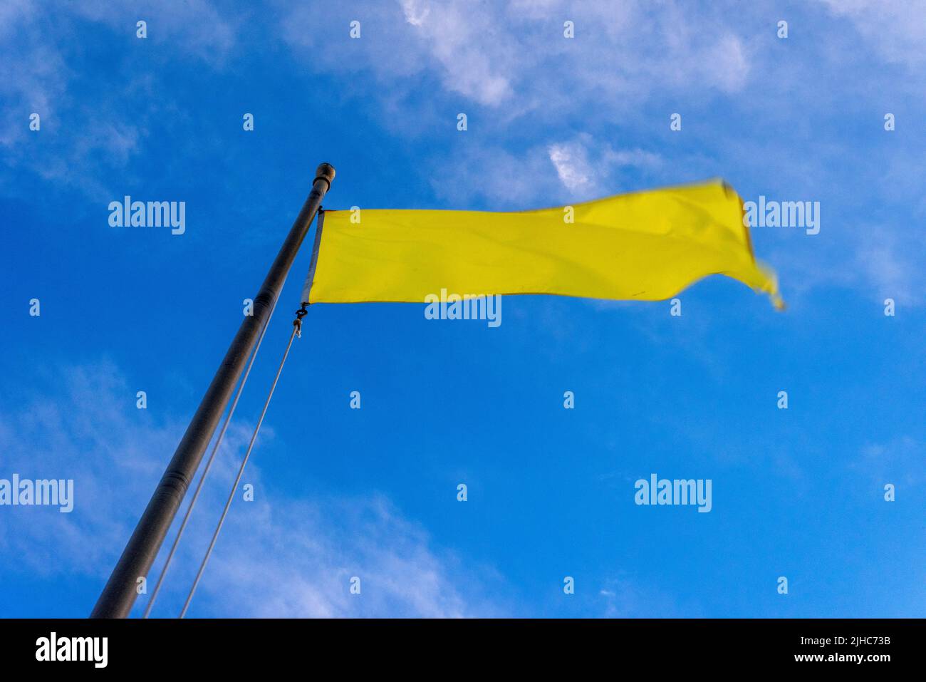A yellow caution flag flaps in the wind warning of hazardous surf ...
