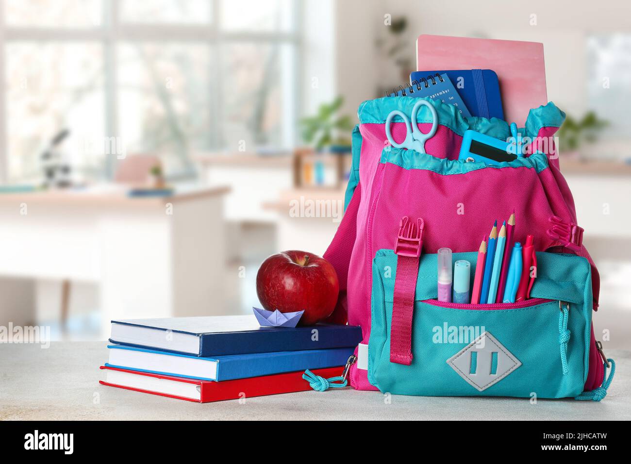 School backpack with stationery, apple and books on table in classroom ...