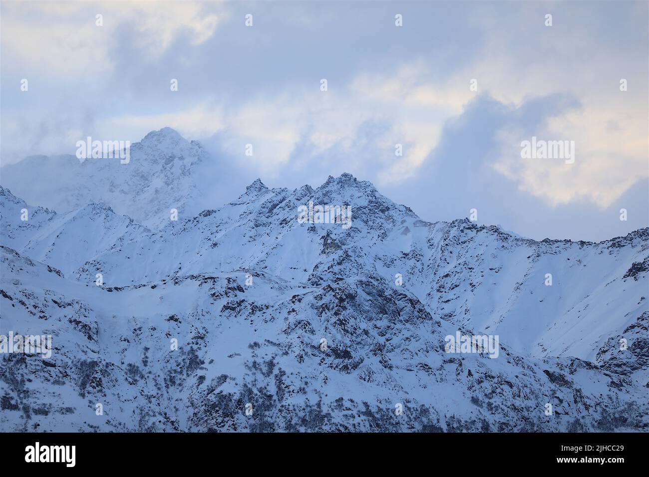 Alaskan snow-covered mountains touch the passing clouds in the cold winter sky Stock Photo - Alamy