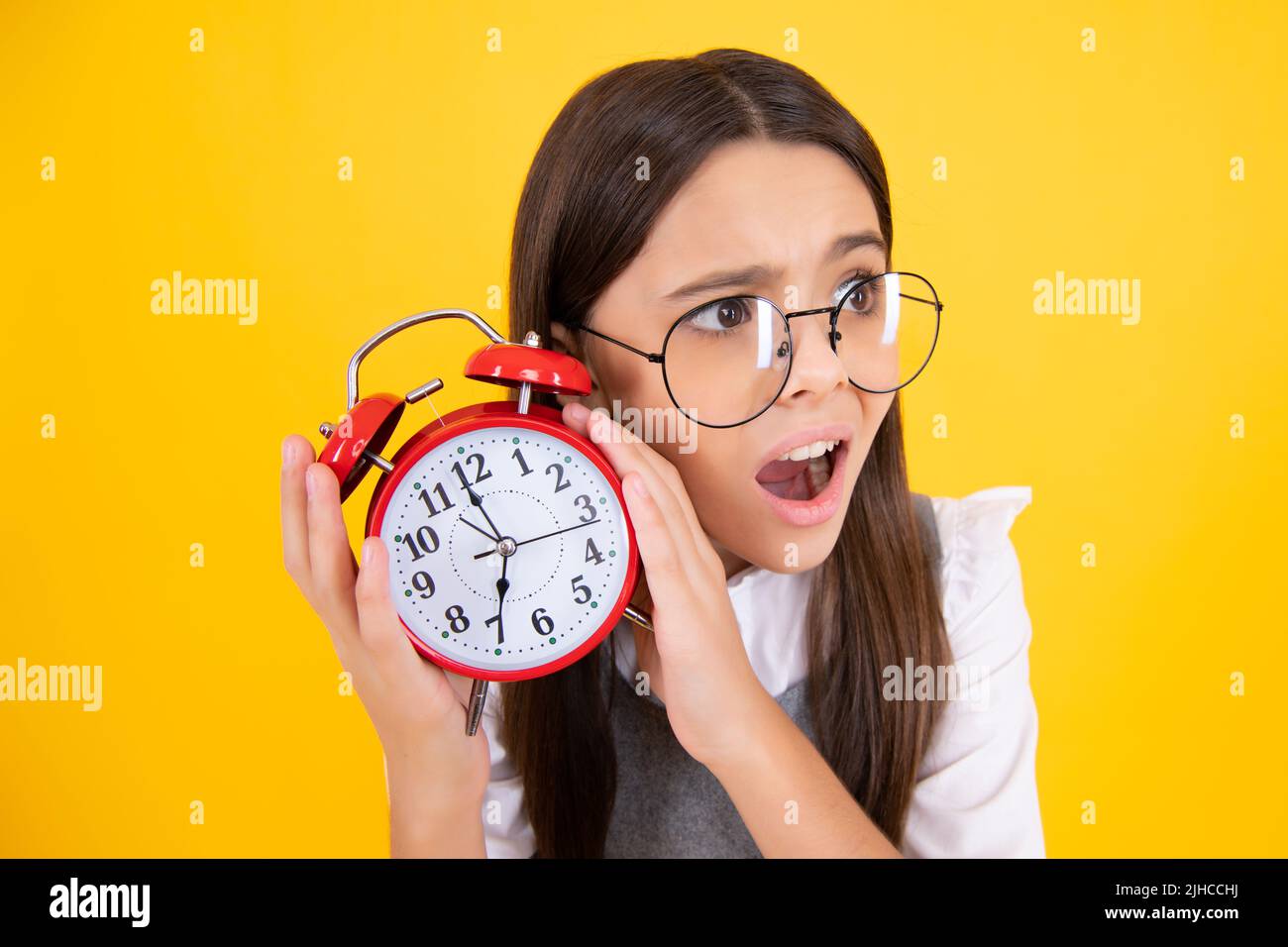 Surprised funny teenager girl child hold clock isolated on yellow ...