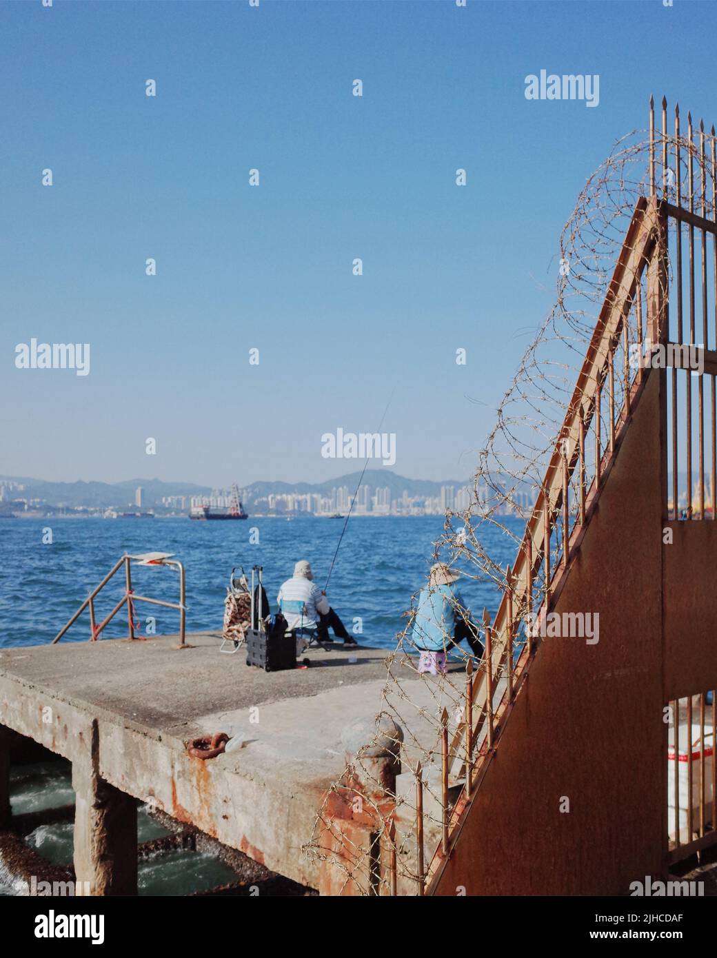 A vertical shot of two people sitting on a concrete platform and ...