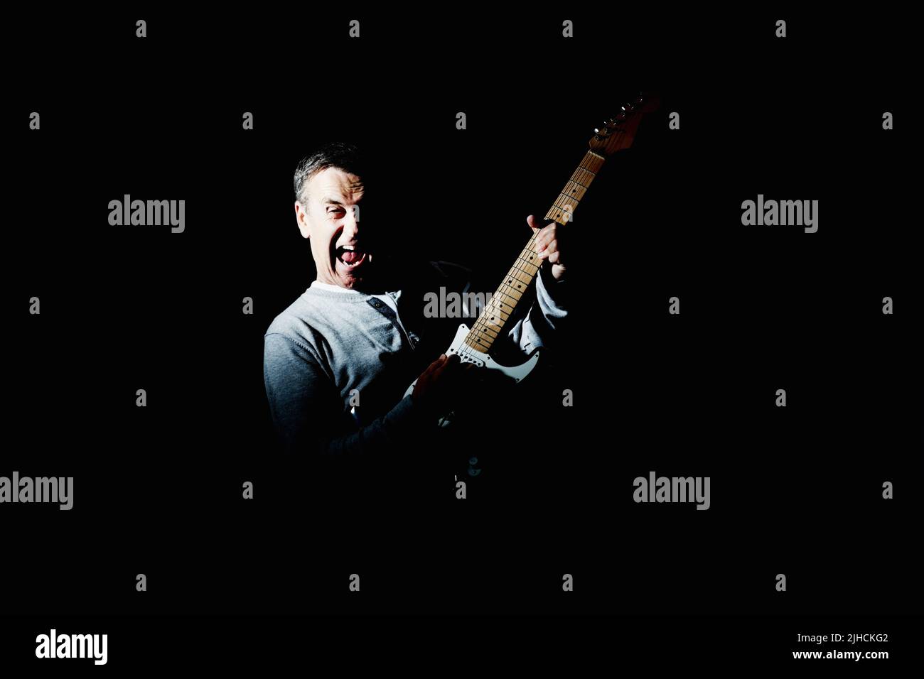 An aggressive man playing guitar against black background. Portrait of ...